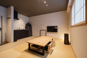 Uma cozinha moderna com armários escuros, uma mesa de jantar de madeira e uma TV embutida.