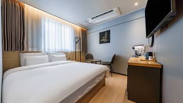Quarto de hotel com uma cama grande, uma escrivaninha com cafeteira, uma cadeira e uma TV fixada na parede.