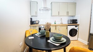 Uma cozinha compacta com área de refeições, com uma mesa redonda, cadeiras amarelas e eletrodomésticos básicos.