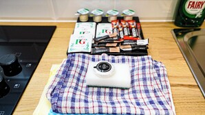 Uma bancada de cozinha com um tecido xadrez, uma cafeteira e diversos alimentos.