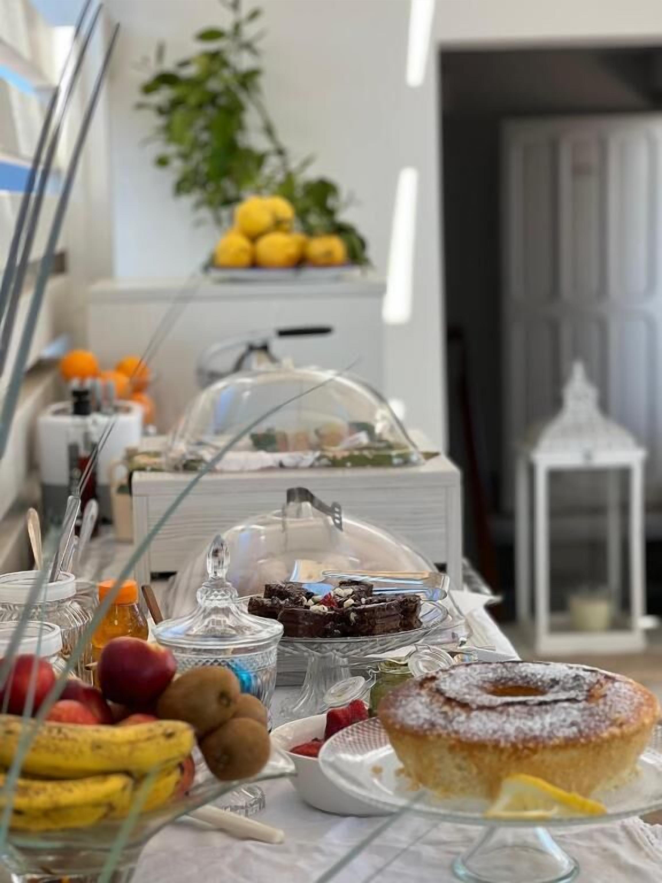 Mesa de buffet com diversos alimentos, incluindo frutas, sobremesas e bebidas.