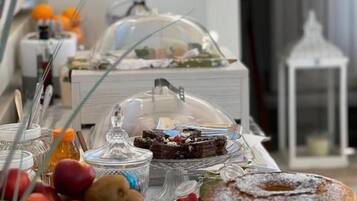 Mesa de buffet com diversos alimentos, incluindo frutas, sobremesas e bebidas.