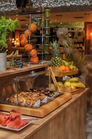 Buffet com diversos alimentos, incluindo frutas, doces e uma exposição de laranjas.