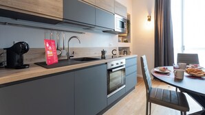 Cozinha moderna com armários cinzentos, forno embutido, cafeteira e mesa de pequeno-almoço com um croissant e chávenas de café.