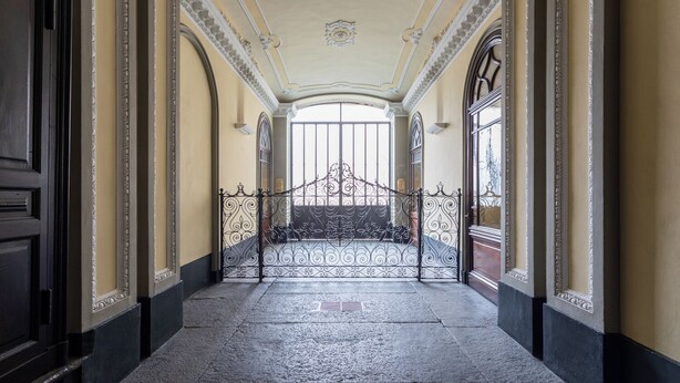 Um corredor com portões de ferro ornamentados, piso de pedra e detalhes arquitetônicos clássicos.