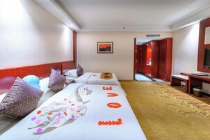 Quarto de hotel com duas camas, televisão, secretária e casa de banho visível através de uma porta aberta.