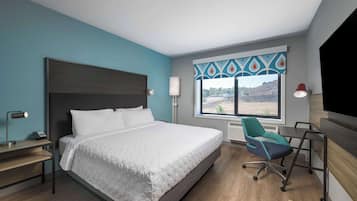 Quarto de hotel moderno com uma cama grande, uma escrivaninha, uma cadeira e uma televisão.