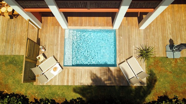 Piscina no terraço com duas espreguiçadeiras e uma mesa, rodeada por deck de madeira e vegetação.