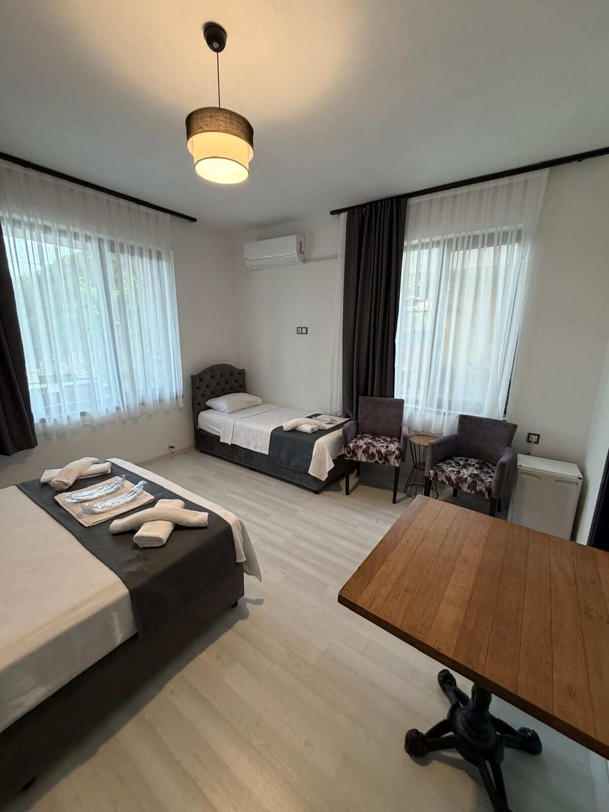 Quarto de hotel com duas camas, uma mesa pequena, uma cadeira, ar condicionado e uma luminária no teto.