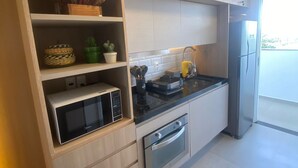 Cozinha moderna com armários de madeira, micro-ondas embutido, forno e geladeira de aço inoxidável.