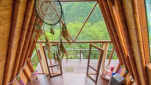 Um quarto com pé-direito alto, decoração em madeira, um sonho apanhado e vista para colinas verdes.