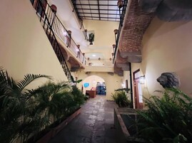 Um átrio com vários níveis, uma escadaria central, soalho de pedra e plantas em vasos.