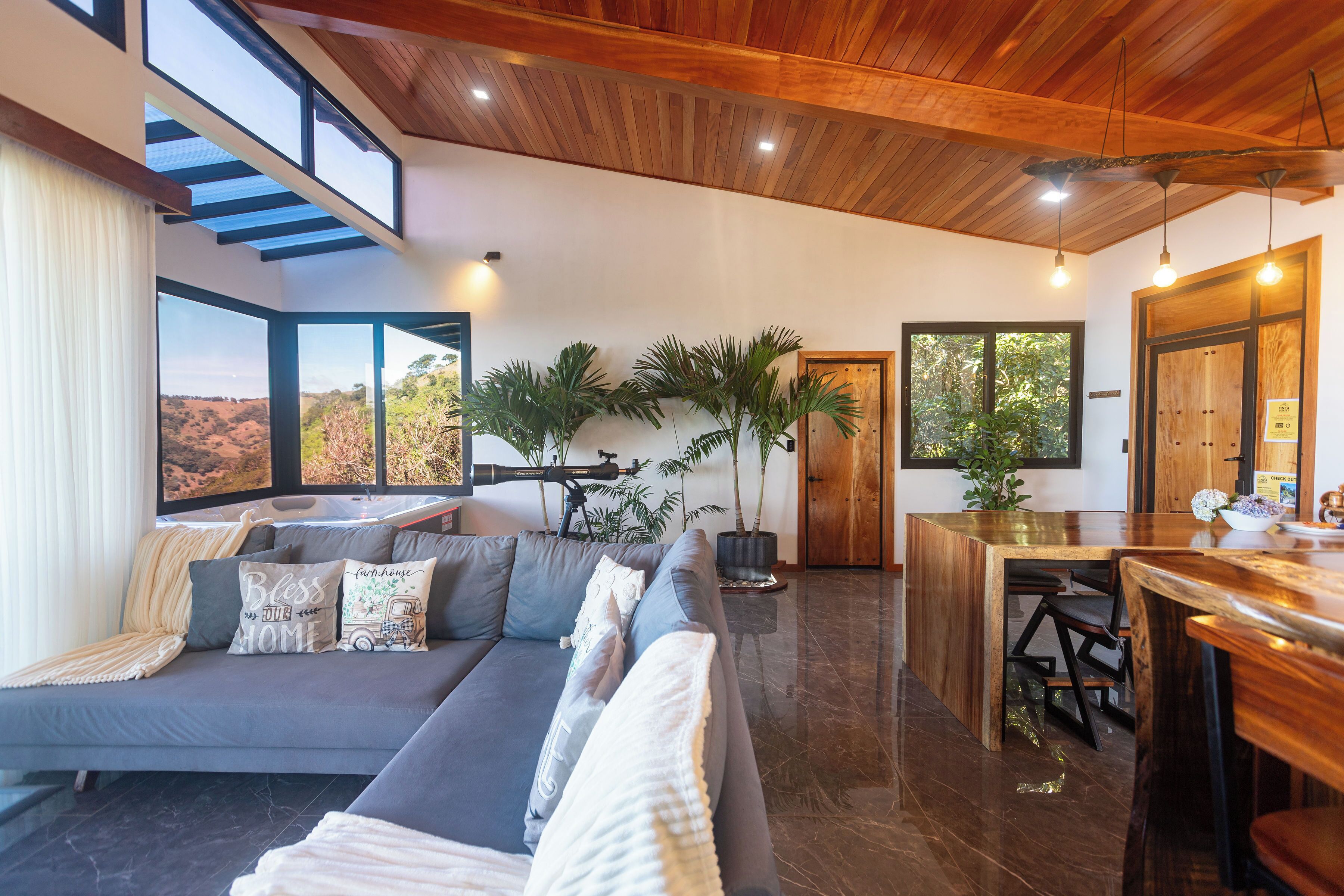 Uma sala de estar moderna com um sofá grande, um espaço de jantar e vista para o exterior.