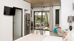 Quarto de hotel moderno com cama, escrivaninha, cadeira, televisão, frigorífico e zona de refeições com mesa e cadeiras.