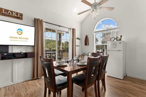 Uma área de refeições com mesa e cadeiras de madeira, um ventilador de teto e vista para o exterior.