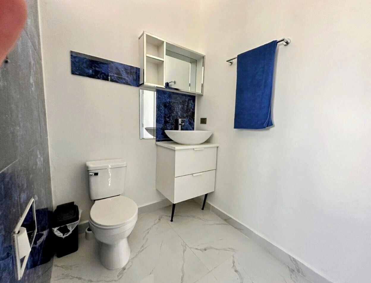 Um banheiro com vaso sanitário, pia com espelho acima e toalha azul pendurada em um suporte.