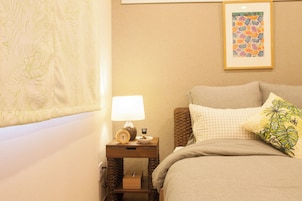 Quarto bem arrumado com uma cama, uma mesinha de cabeceira com luminária, relógio e um quadro na parede.