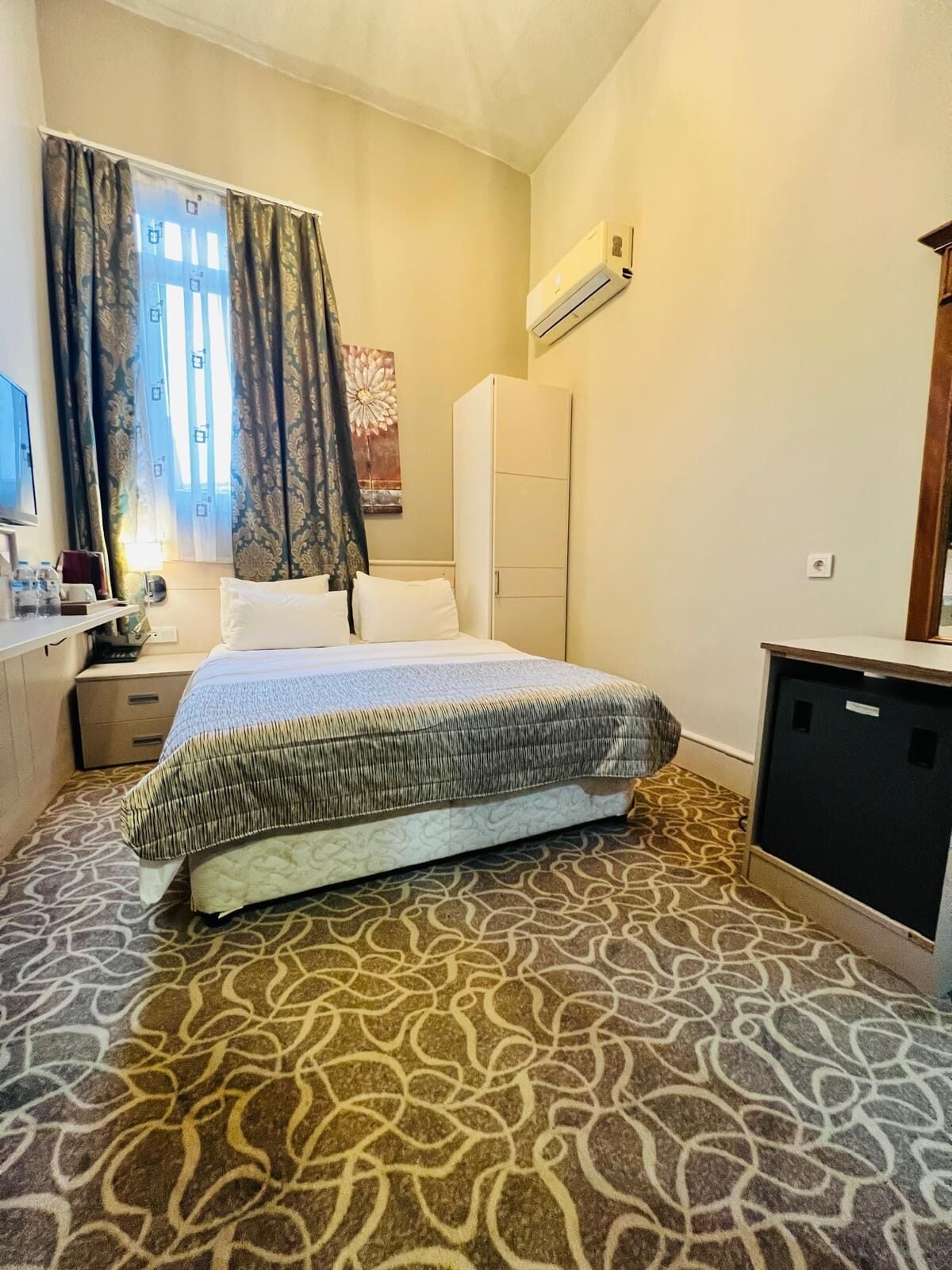 Quarto de hotel com uma cama, guarda-roupa, escrivaninha com luminária e televisão.