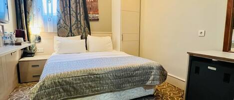 Quarto de hotel com uma cama, guarda-roupa, escrivaninha com luminária e televisão.