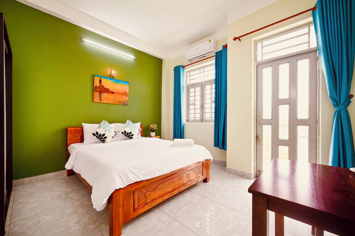 Quarto com cama de madeira, paredes verdes, um quadro e uma janela com cortinas.
