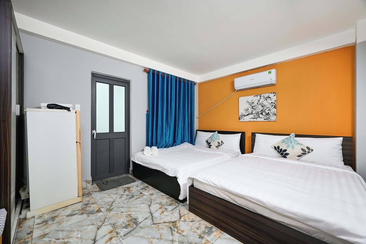 Quarto de hotel com duas camas, geladeira, porta e ar condicionado.