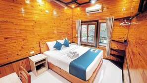 Quarto de cabana de madeira com cama, uma mesinha e janela com cortinas.