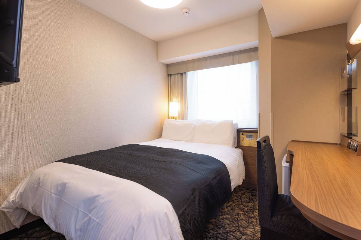 Quarto de hotel com cama, escrivaninha e cadeira.