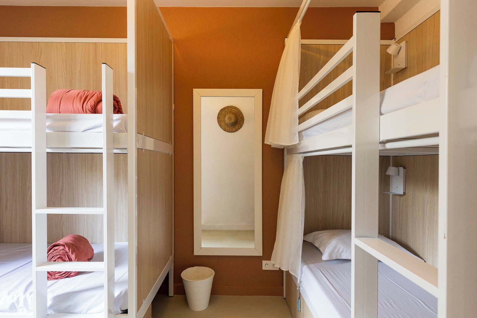 Quarto compacto com beliches, uma janela pequena e luminária fixada na parede.