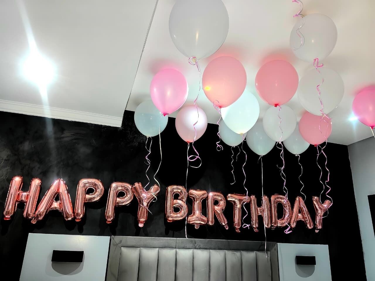 Quarto decorado com um balão de 'FELIZ ANIVERSÁRIO' e uma parede preta.