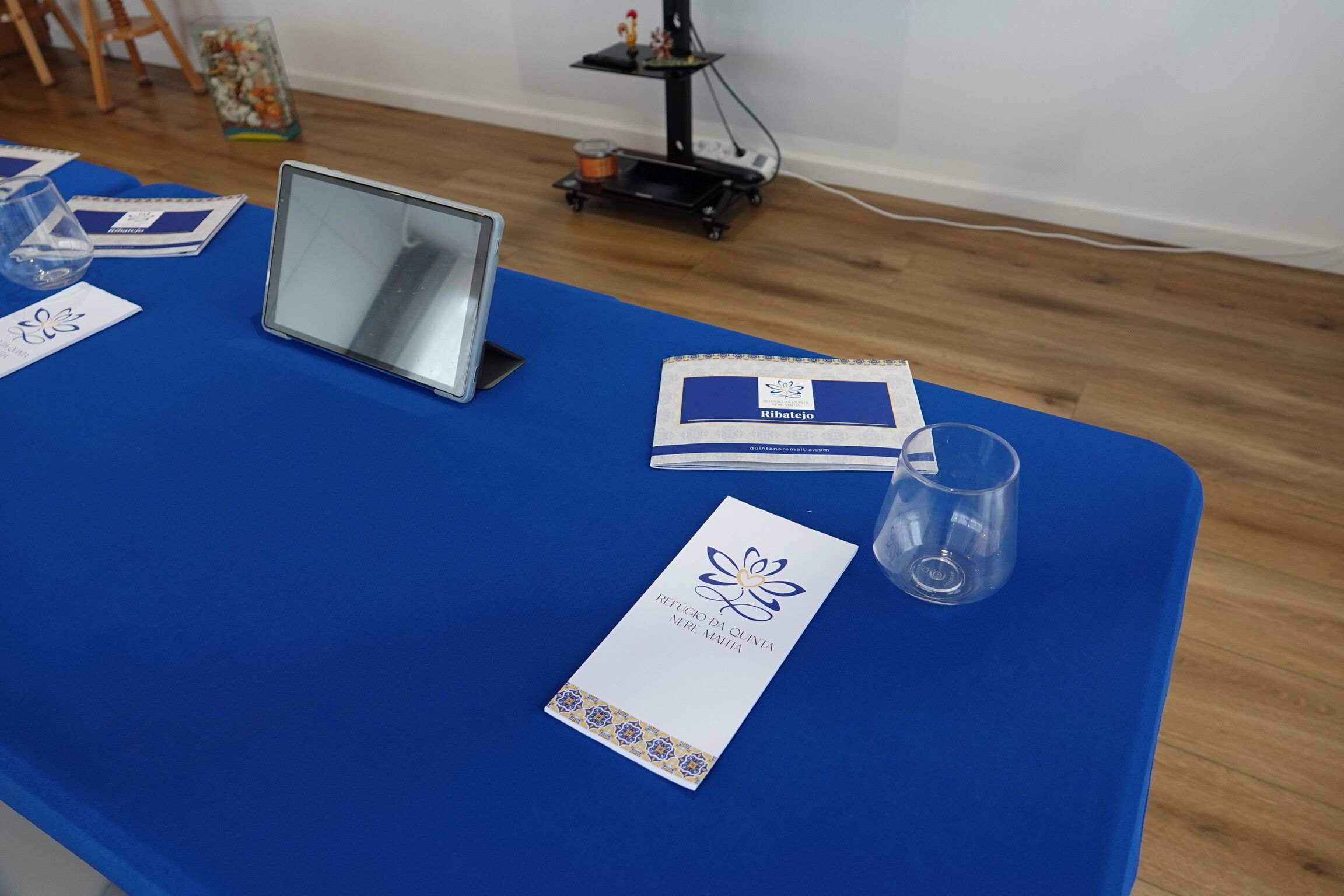 Uma mesa com toalha azul, um laptop, um caderno, um copo e um cartão com texto.