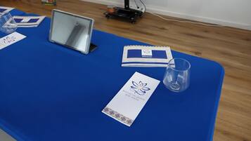 Uma mesa com toalha azul, um laptop, um caderno, um copo e um cartão com texto.