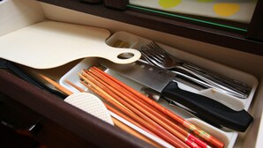 Uma gaveta com utensílios de cozinha, incluindo palitos asiáticos, tábua de corte e faca.