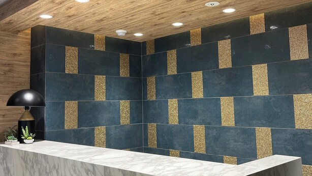 Uma receção com bancada de mármore, rodeada por azulejos azul escuro com detalhes dourados, vigas de madeira no teto e iluminação embutida.