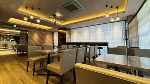 Interior moderno de restaurante com piso de madeira, várias mesas e cadeiras, iluminação pendente e parede com padrão herringbone.