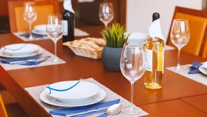 Uma mesa de jantar posta com pratos, talheres e copos de vinho, com uma garrafa de vinho e uma pequena planta sobre a mesa.