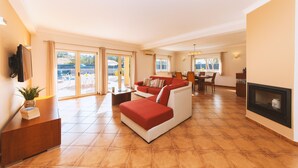 Uma sala de estar espaçosa com sofá vermelho e branco, lareira e área de jantar com mesa e cadeiras.