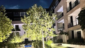 Um edifício moderno com várias varandas, um caminho central e vegetação bem cuidada.