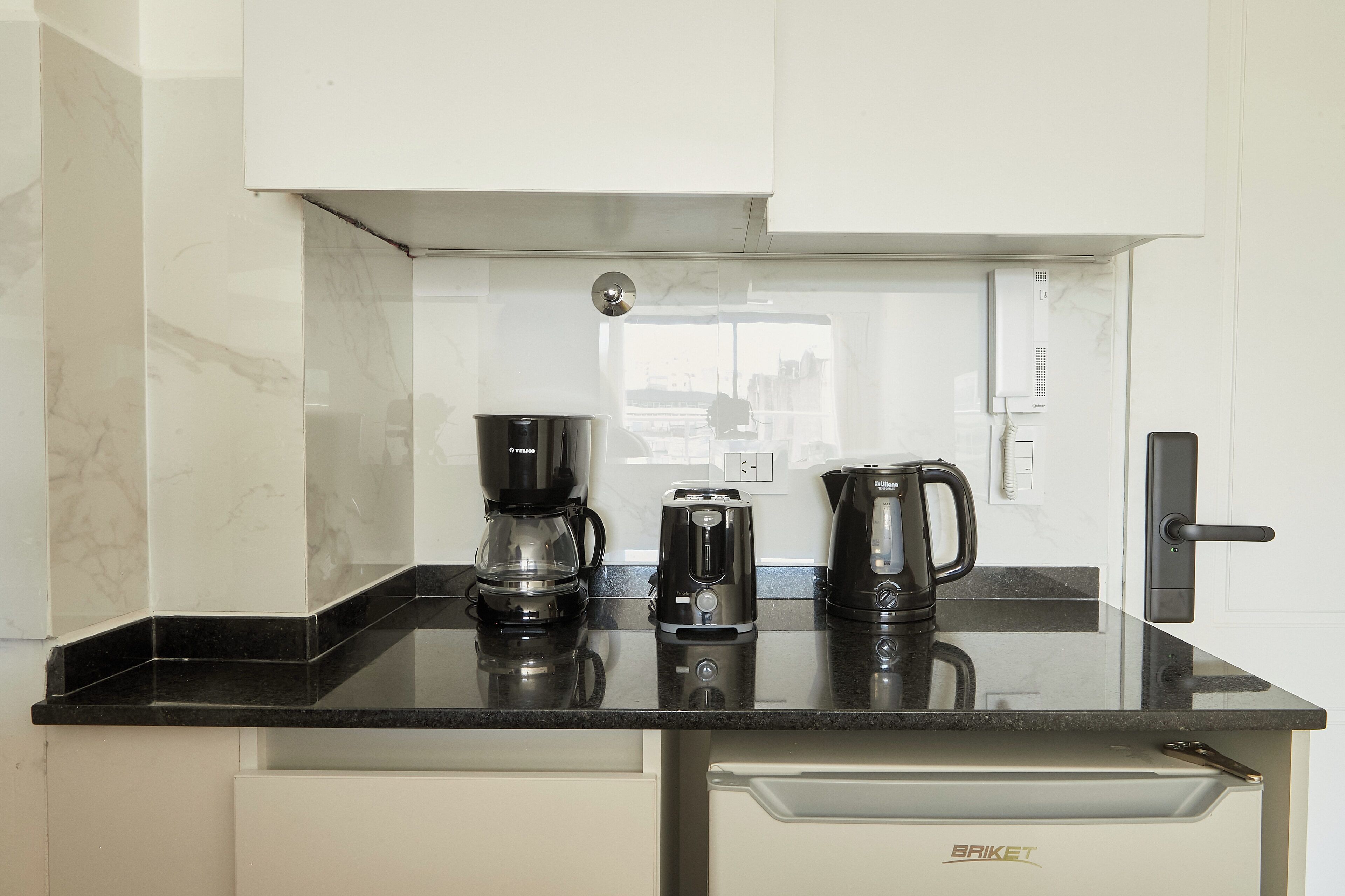 Cozinha com bancada preta, cafeteira, torradeira e chaleira.