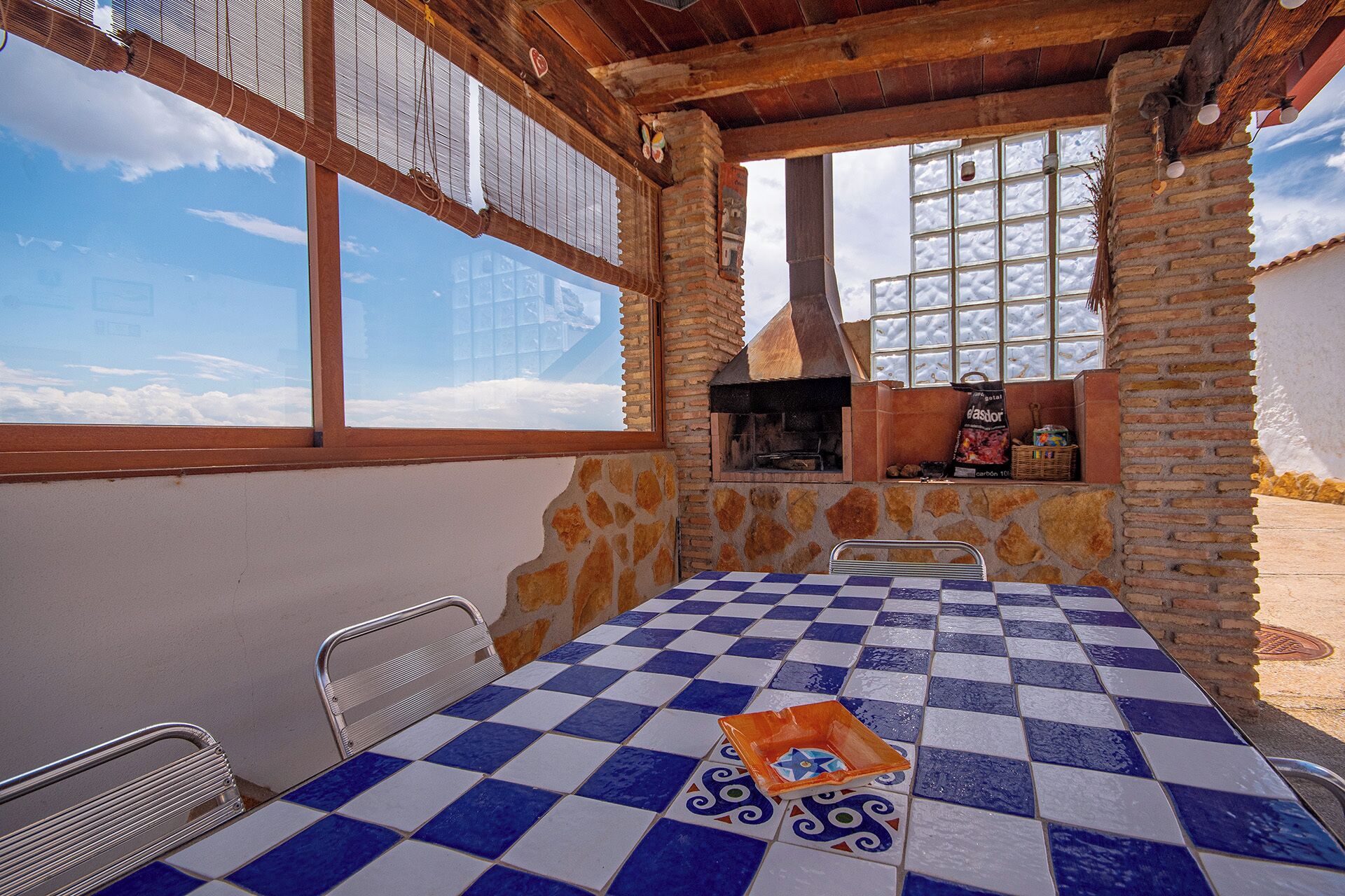 Um pátio externo com uma mesa xadrez, um forno de tijolos e vista para o céu.