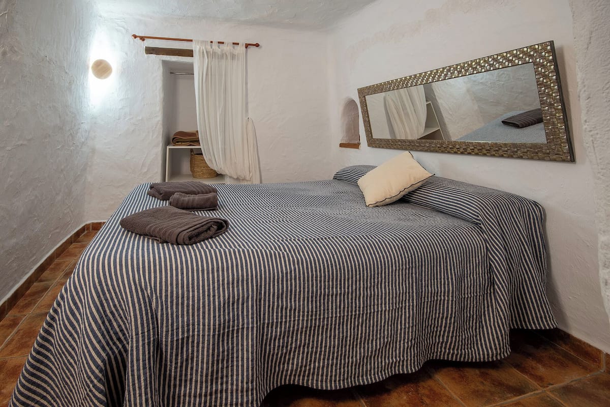 Quarto com cama, espelho e janela com cortinas.