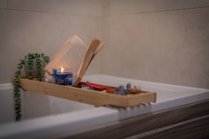 Uma banheira com um tabuleiro de madeira contendo um livro, uma vela e produtos de banho.