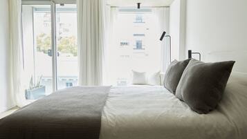 Quarto com cama, janela e vista para prédios.