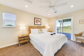 Quarto com cama grande, duas luminárias de cabeceira, mesa de cabeceira de madeira, ventilador de teto, janela e varanda com vista.