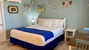 Quarto com cama, mesa de cabeceira, cadeira e parede decorada com uma placa de surf, uma placa de praia e um salva-vidas.