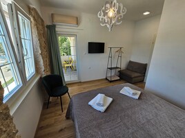 Quarto com cama, cadeira, sofá, televisão e janela com cortinas.