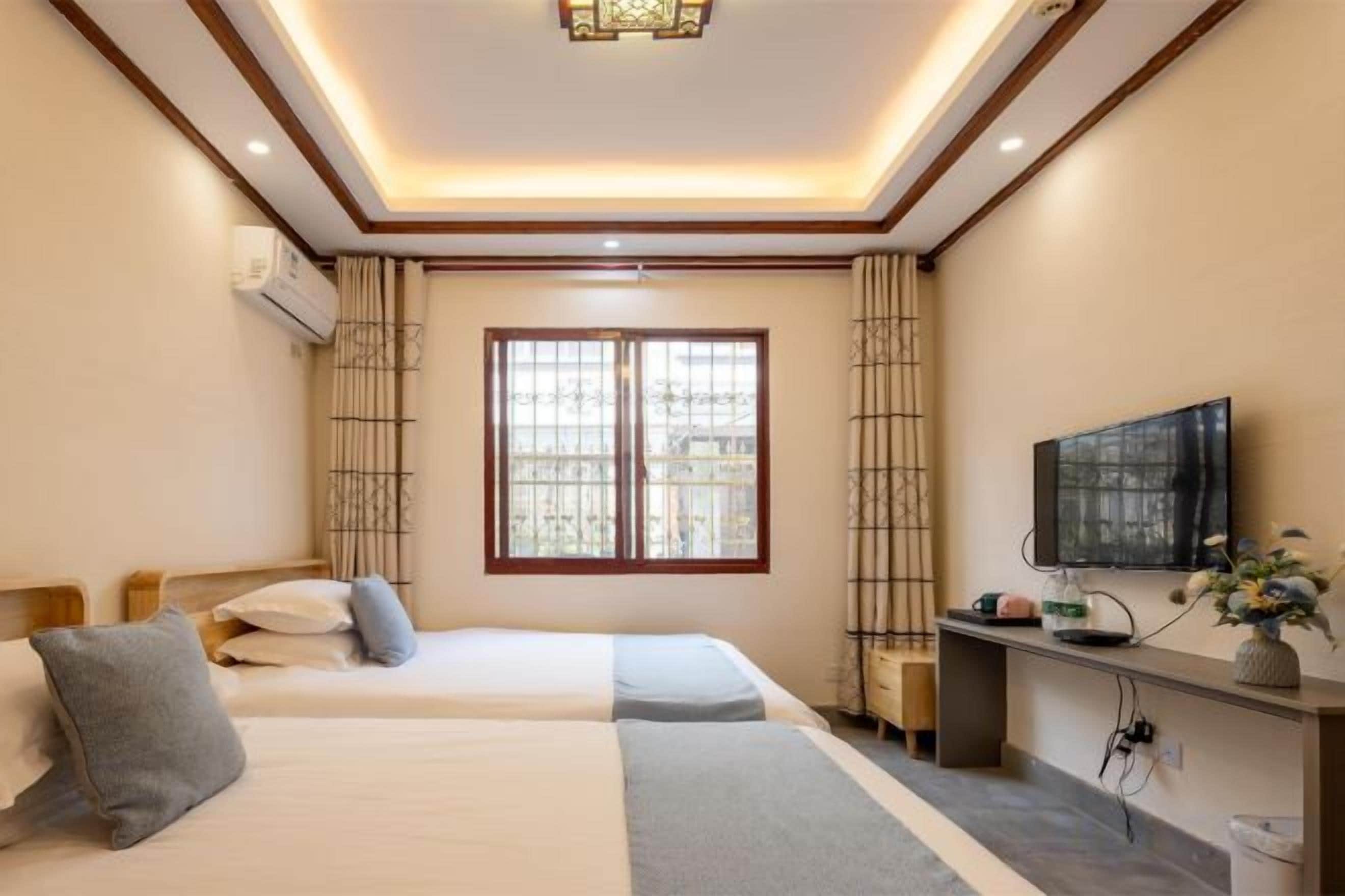 Quarto de hotel com duas camas, televisão, escrivaninha com computador e janela com vista.