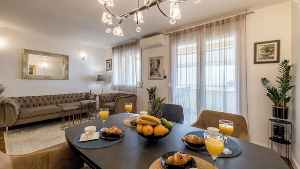 Uma área de refeições com uma mesa posta para o café da manhã, incluindo croissants, frutas e suco de laranja.