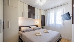 Quarto moderno com cama grande, armário embutido, abajures e televisão de tela plana.