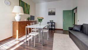 Uma sala de estar moderna com área de jantar, sofá, porta verde e uma pintura com paisagem urbana.