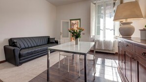 Uma sala de estar moderna com uma mesa de jantar de vidro, um sofá de couro preto e um armário de madeira com uma luminária.